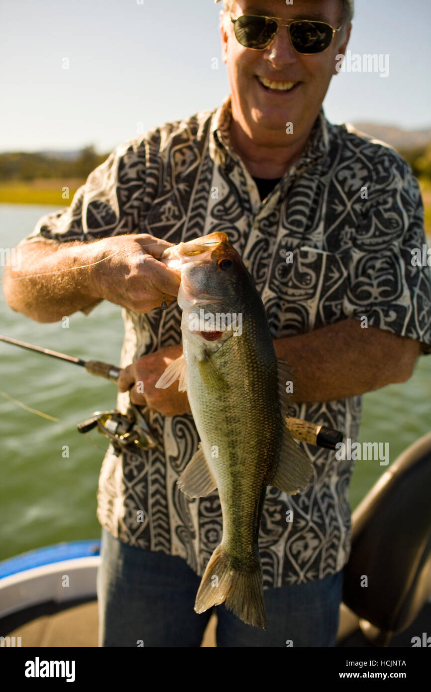 A man holds up his catch proudly for the camera while bass fishing in ...