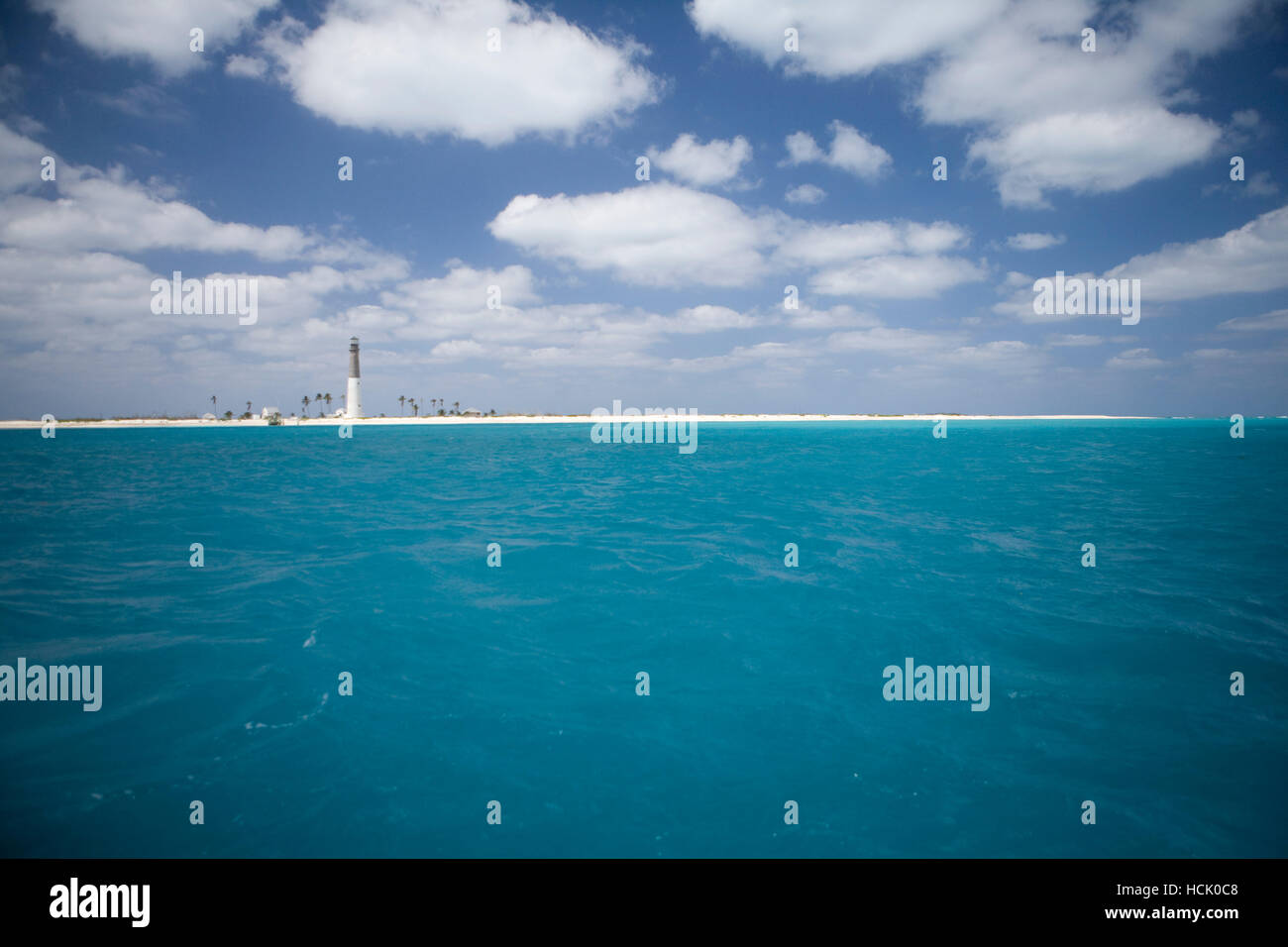 A far off view of an island with a lighthouse with puffy white clouds ...