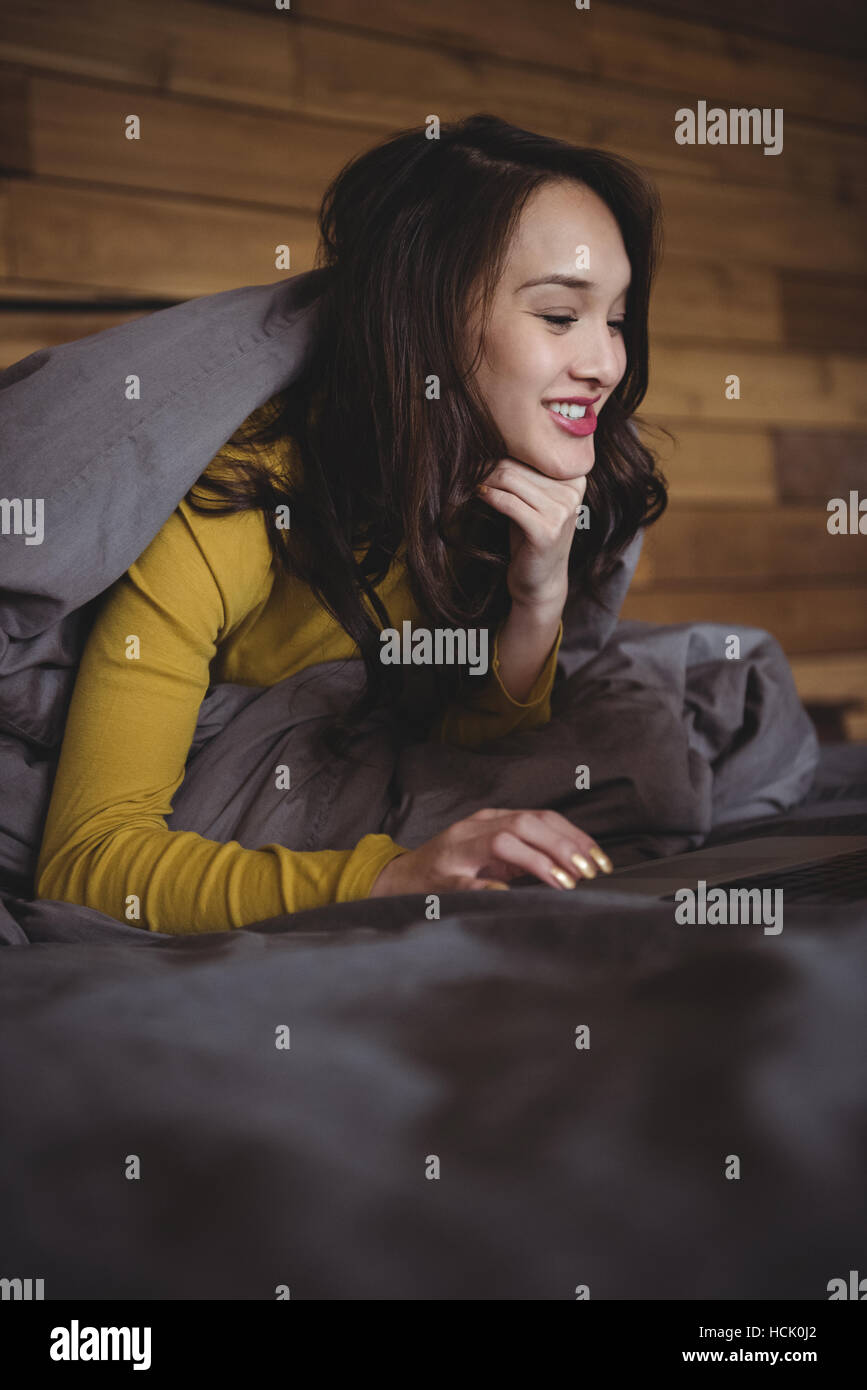 Smiling woman lying on bed using laptop in bedroom Stock Photo - Alamy