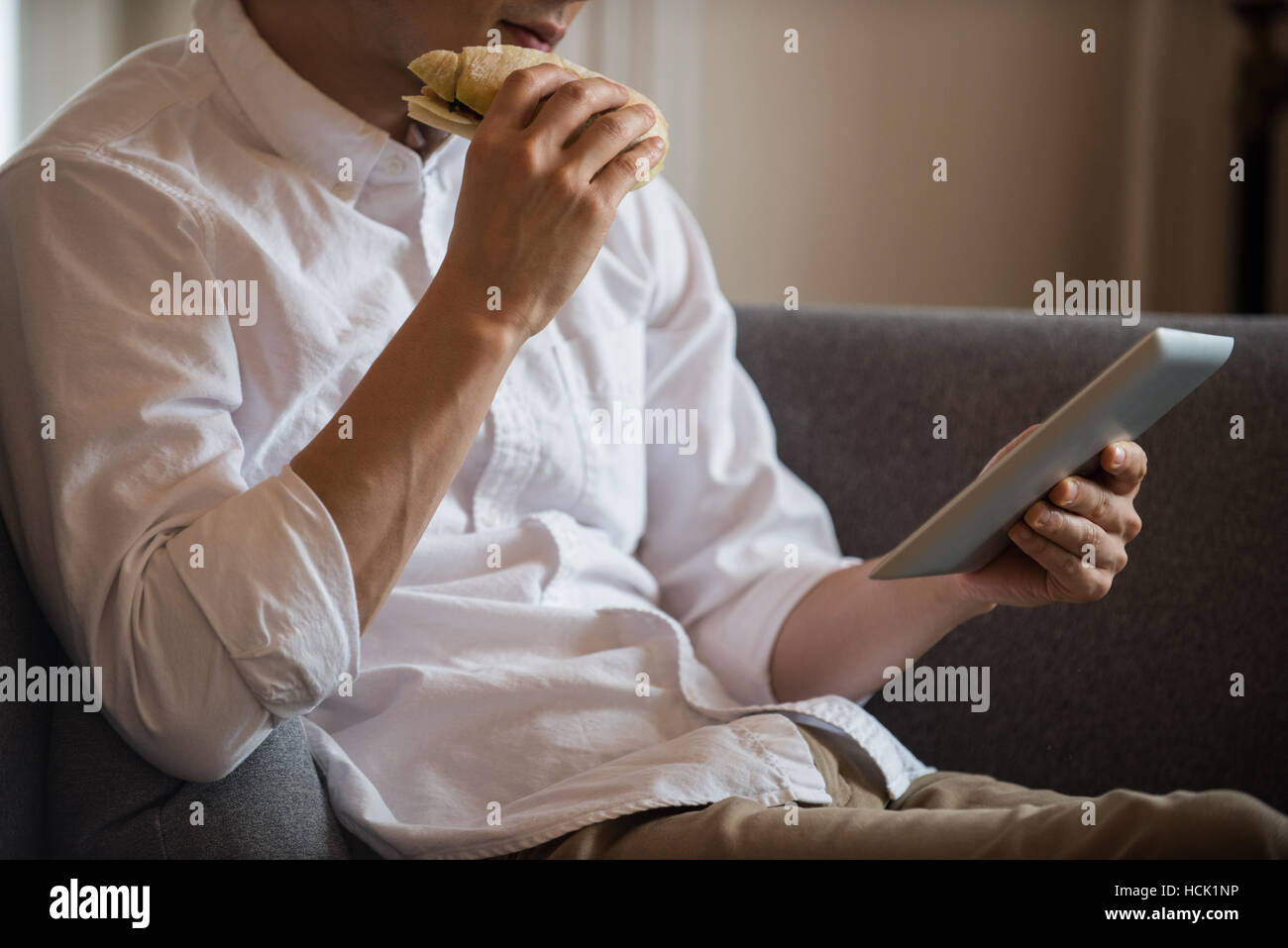 Man using digital tablet while having sandwich Stock Photo - Alamy