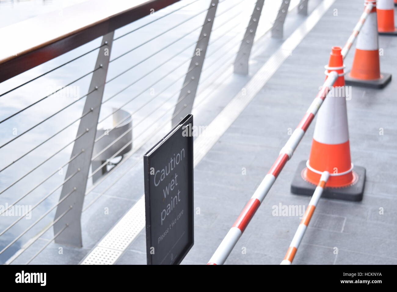 Black caution sign pinned to the railings on a bridge with cones on the ...