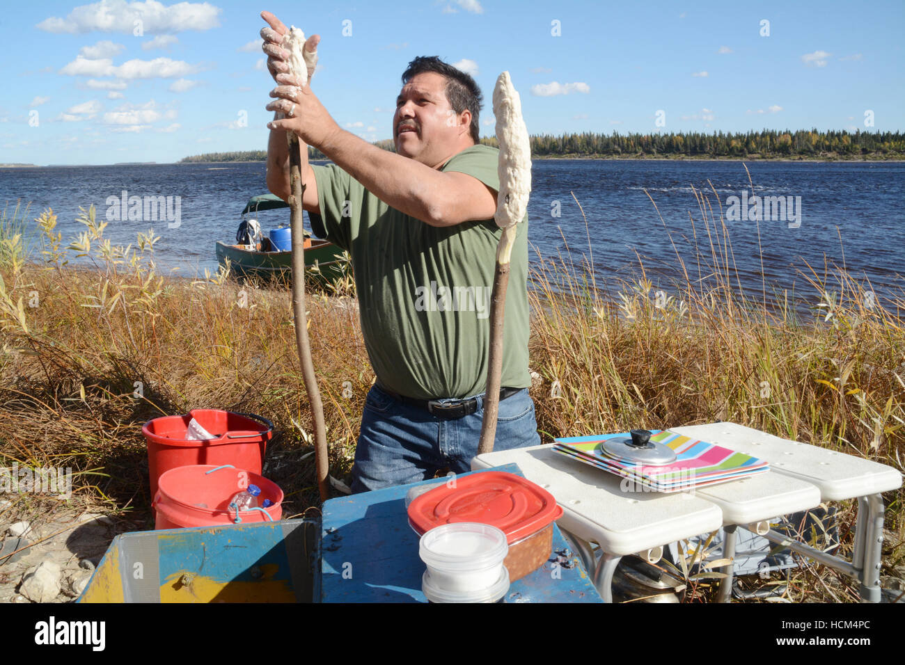 An indigenous man making bannock on a stick, a native North American ...