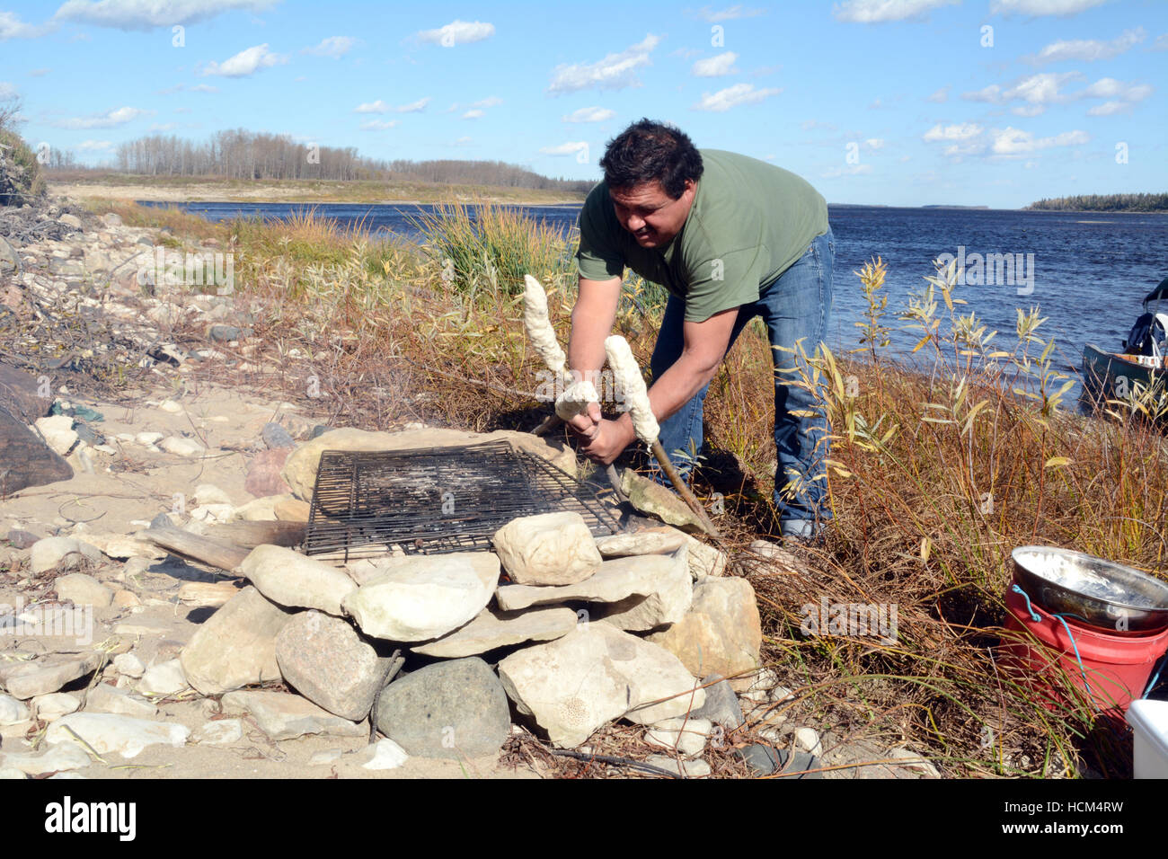 An indigenous man making bannock on a stick, a native North American ...