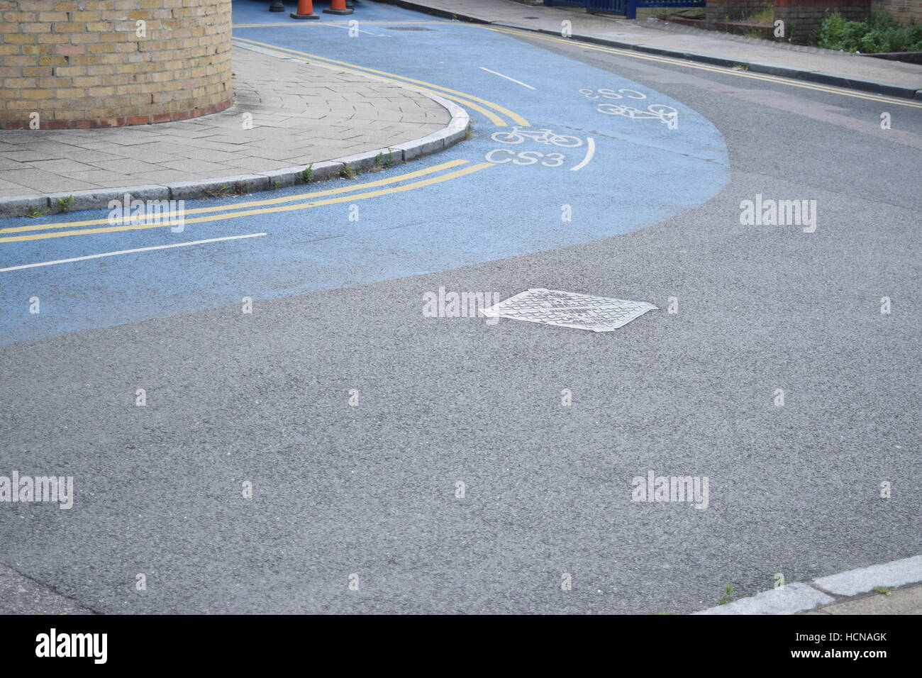Blue bicycle lane on a corner road next to a brick wall Stock Photo - Alamy