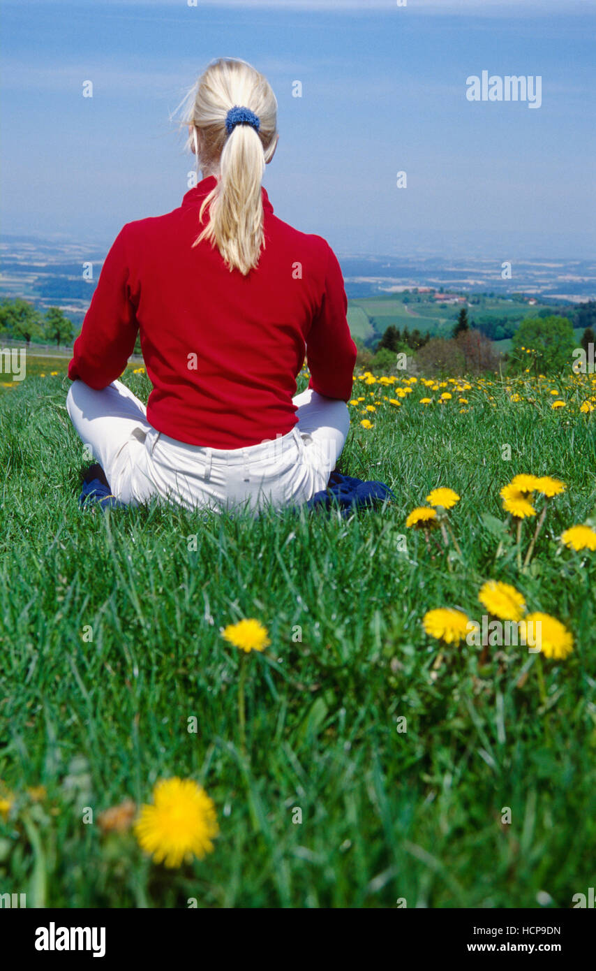 Blonde woman wearing a red sweater, sitting in a meadow, view from ...