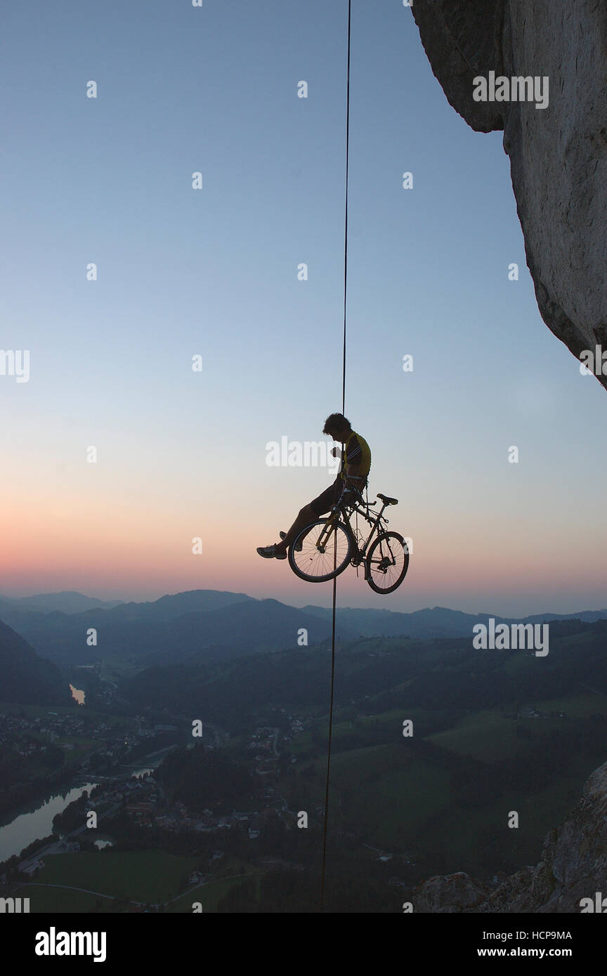 Extreme sport, a man abseiling with a bike in front of the sunset ...