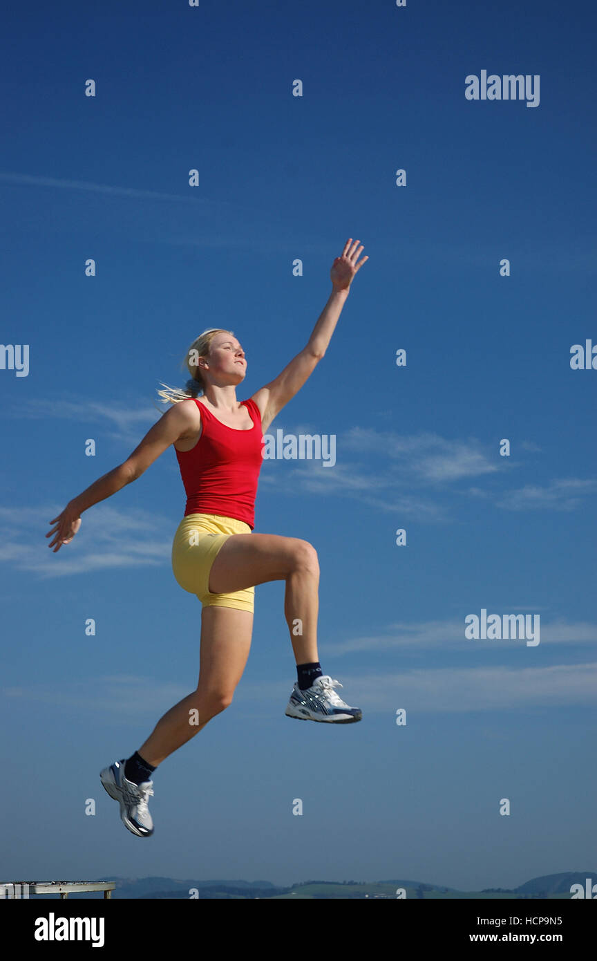 Young blonde woman jumping in the air whilst running Stock Photo - Alamy
