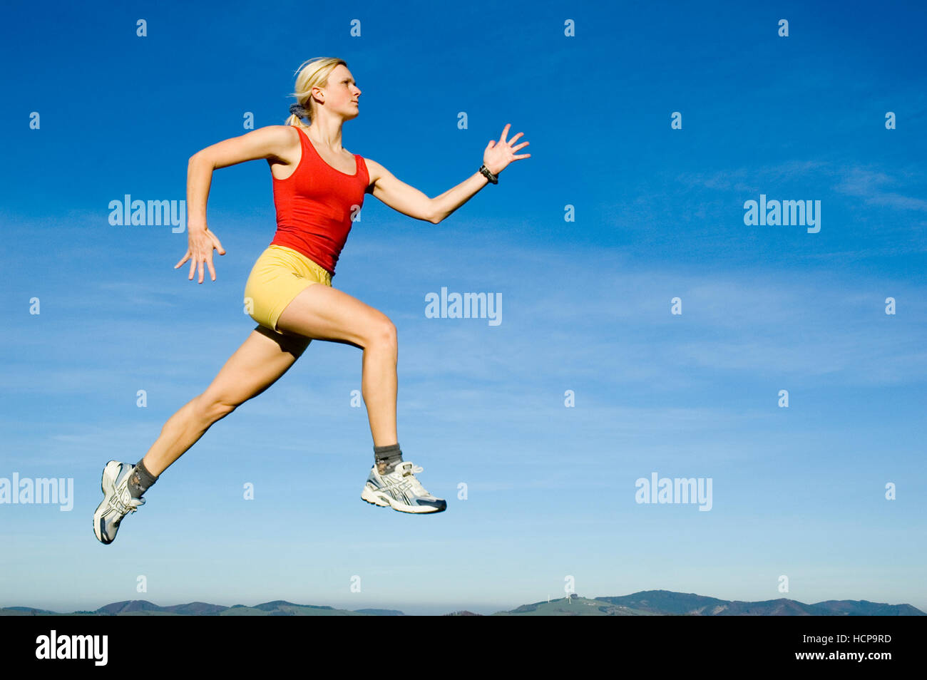 Young blonde woman jumping in the air whilst running Stock Photo - Alamy