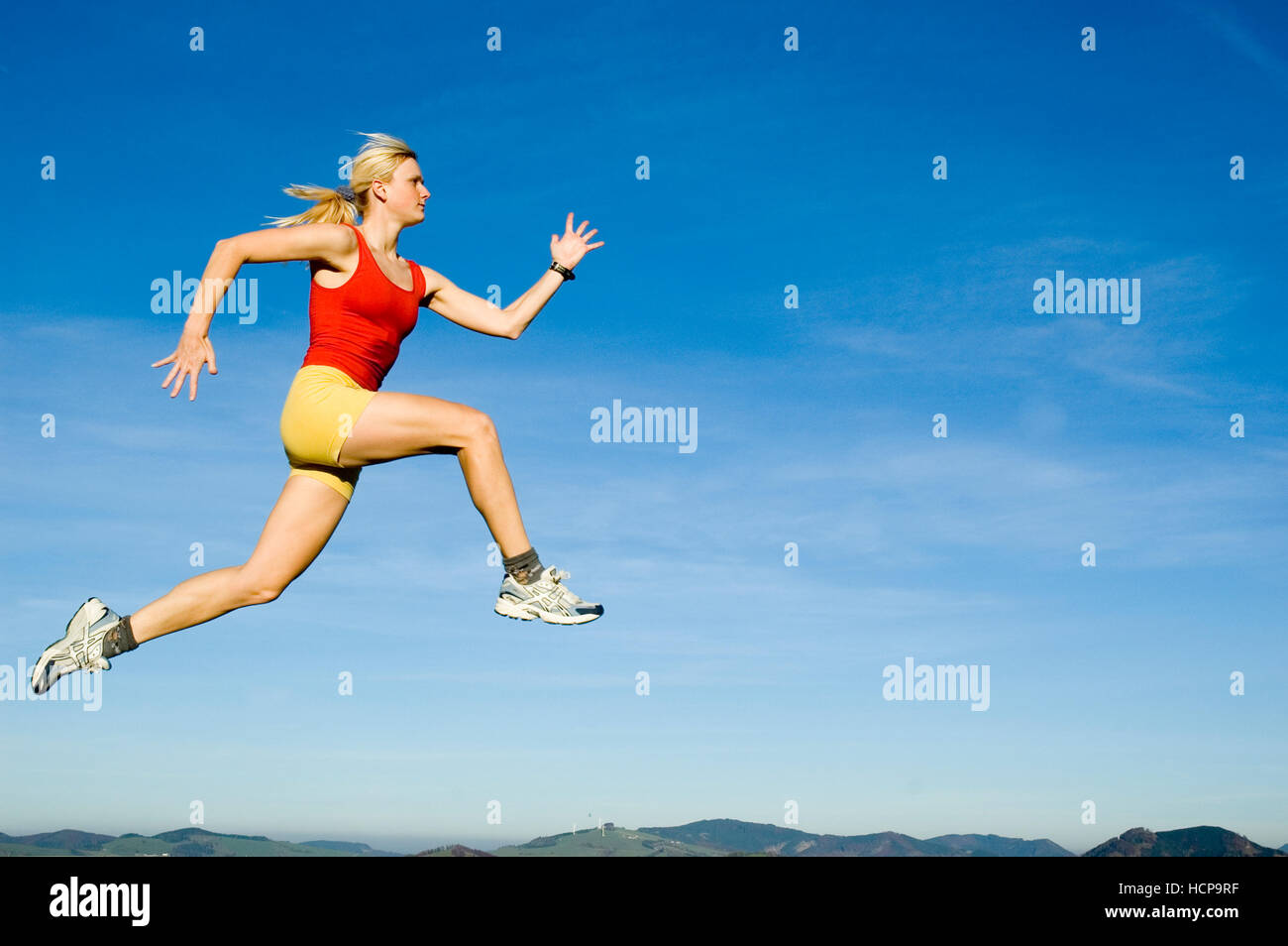 Young blonde woman jumping in the air whilst running Stock Photo - Alamy