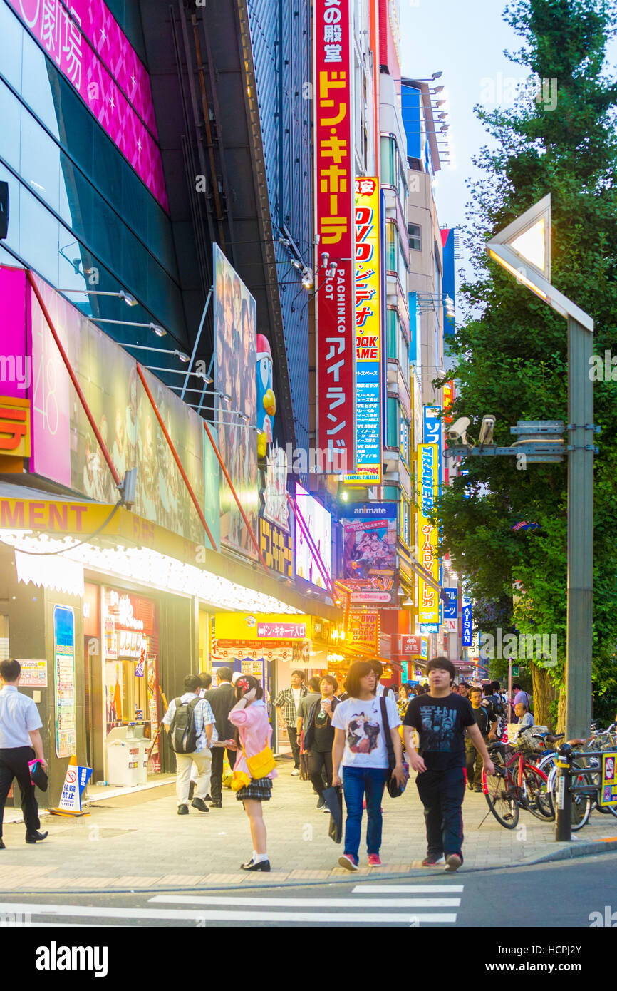 People walking on sidewalk under vertical store signs and bright lights ...