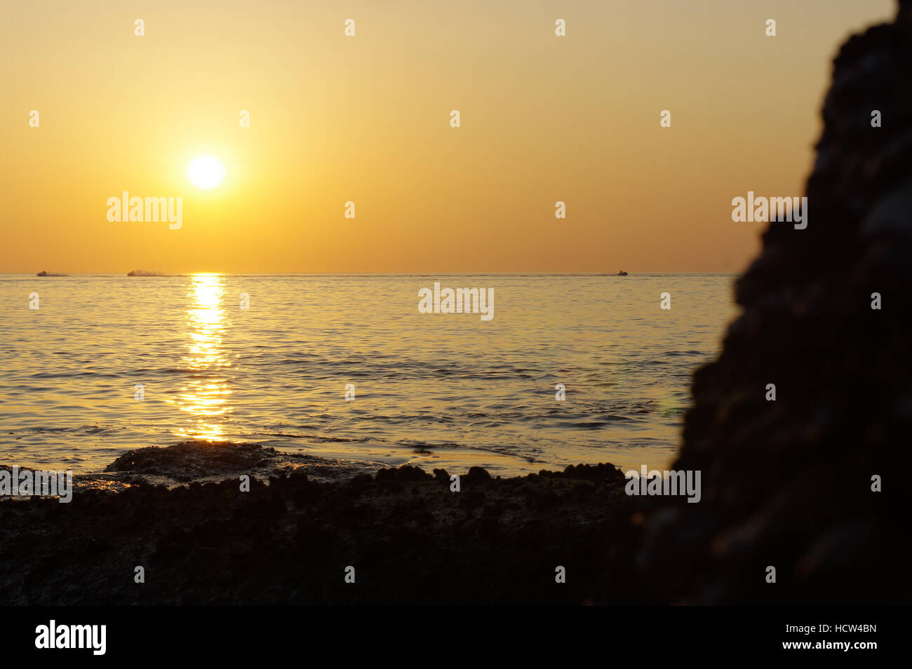 a Vivid orange sunset over water, with rock silhouettes. Thailand ...