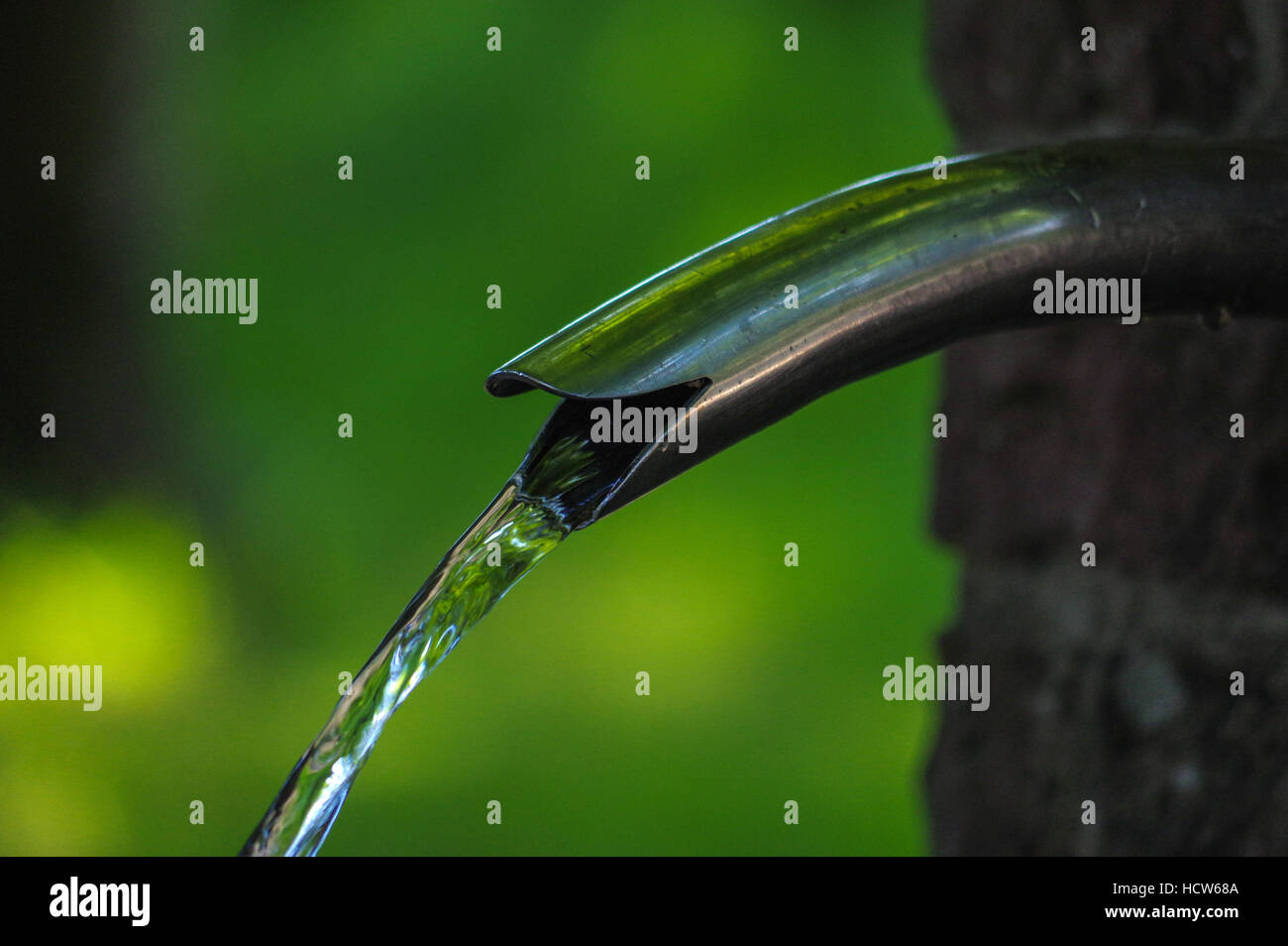 Close up of running water from a tap with brick wall on green ...