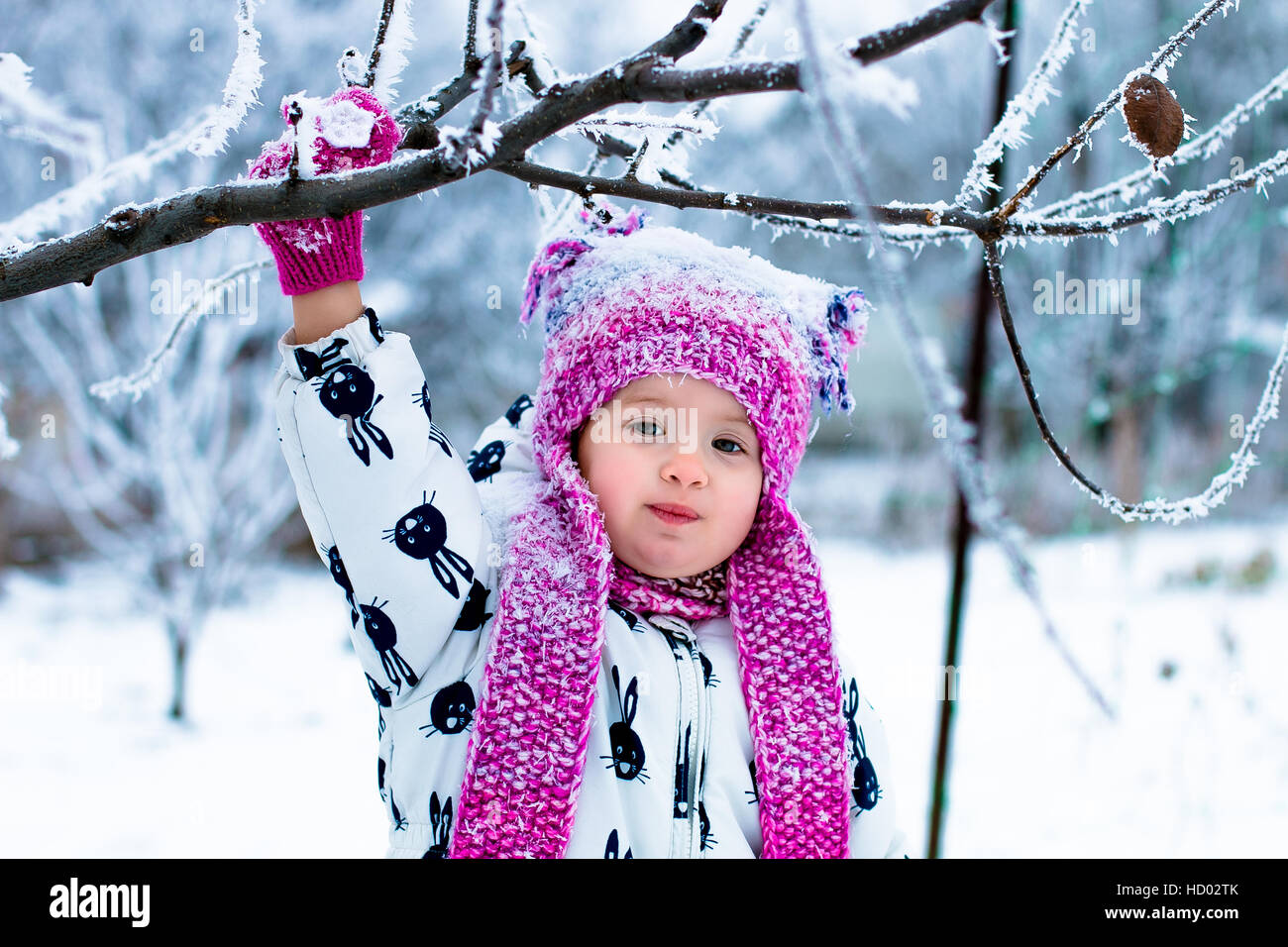 Child in snowy day. Baby girl in white snowsuite and pink hat, boots ...