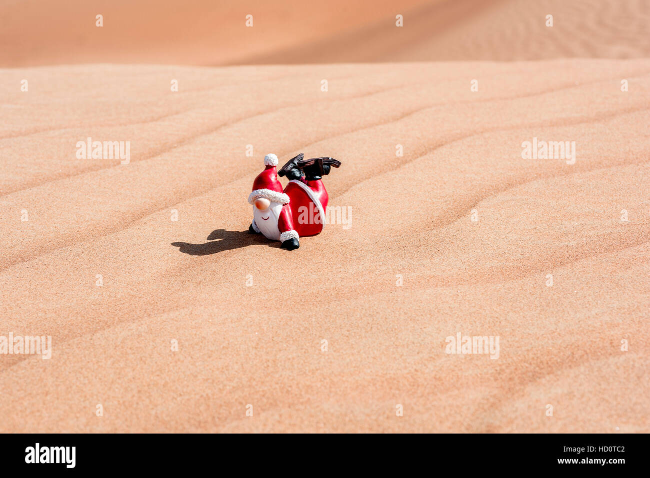 Santa Claus figurine comically sliding on desert sand, blending festive ...