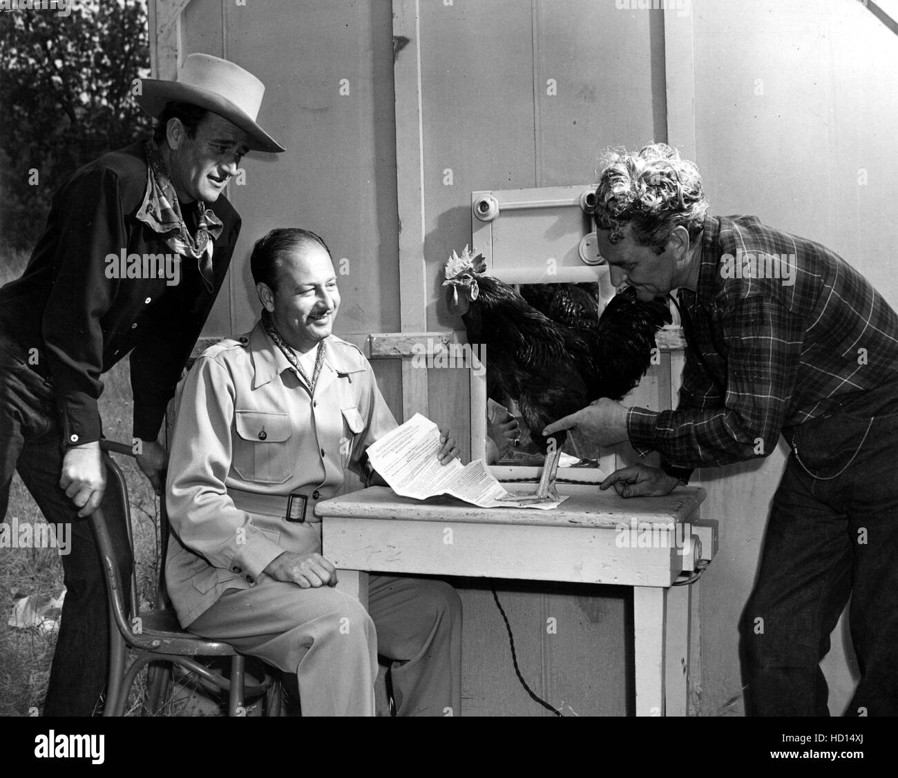 John Wayne, director Edwin Marin and prop man Earl McKee on the set of ...
