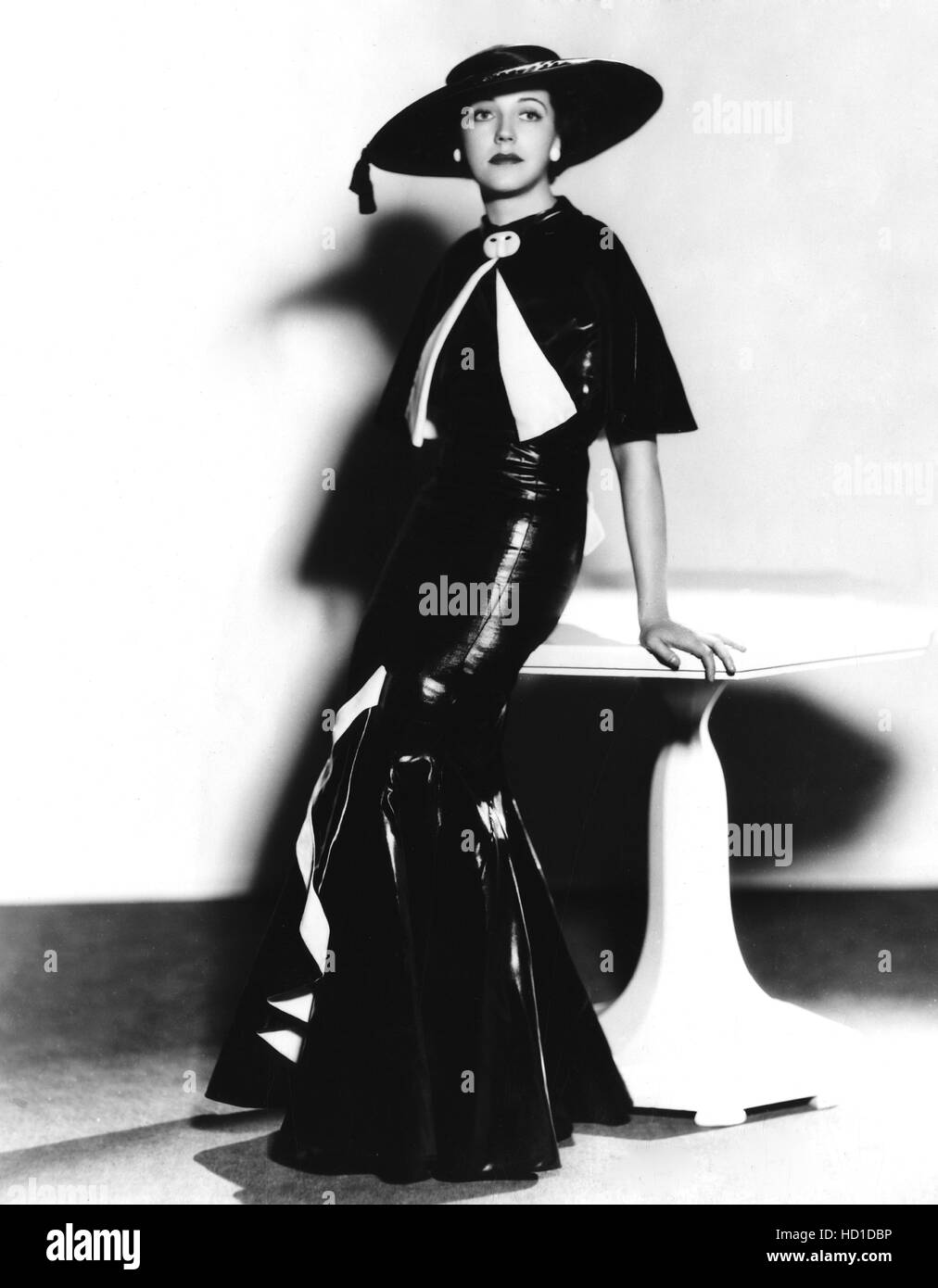 Mona Barrie, in a gown of black glazed satin with cape and white waffle ...