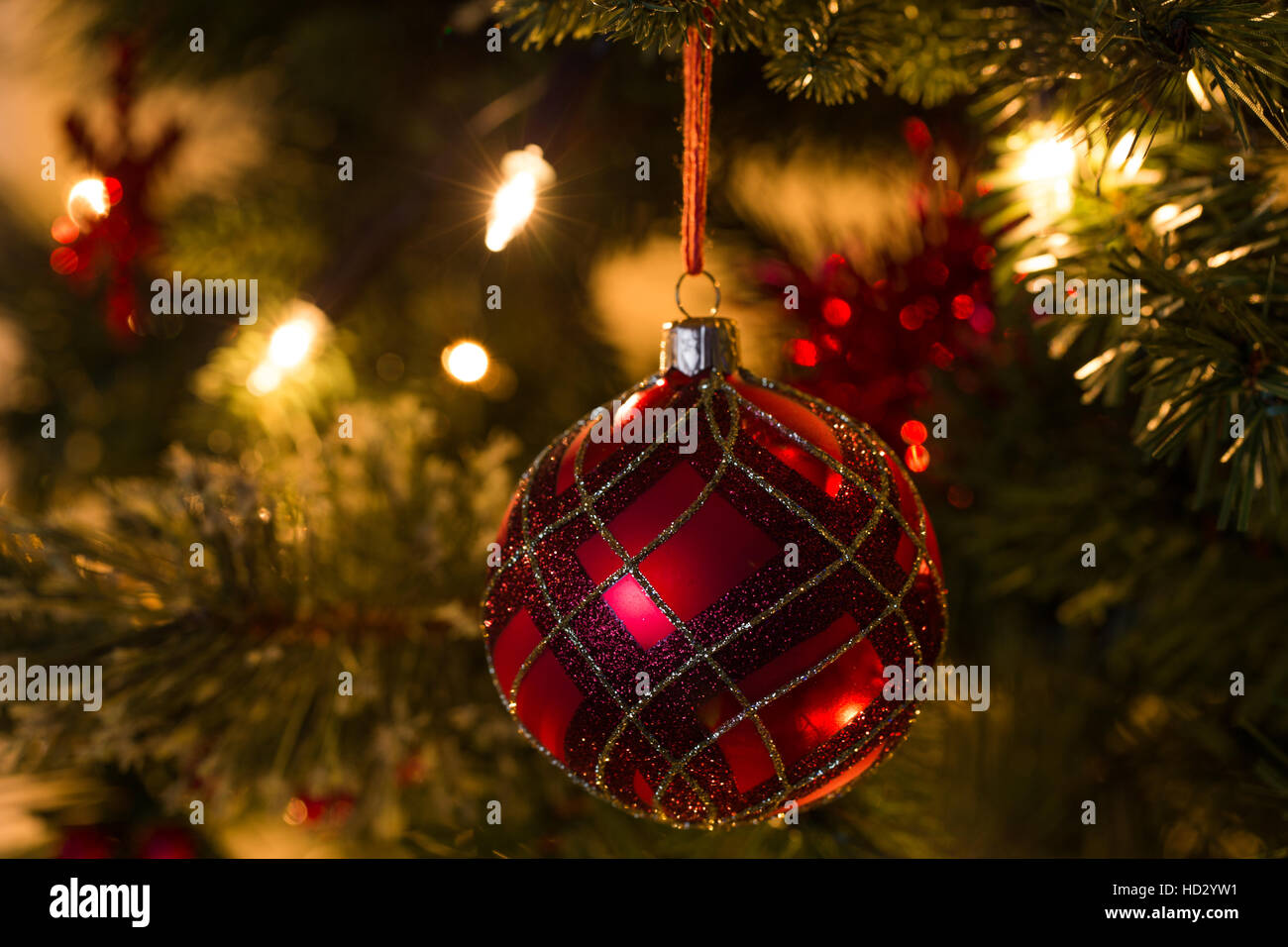 A red christmas bauble hangs on a tree with fairy lights behind it ...