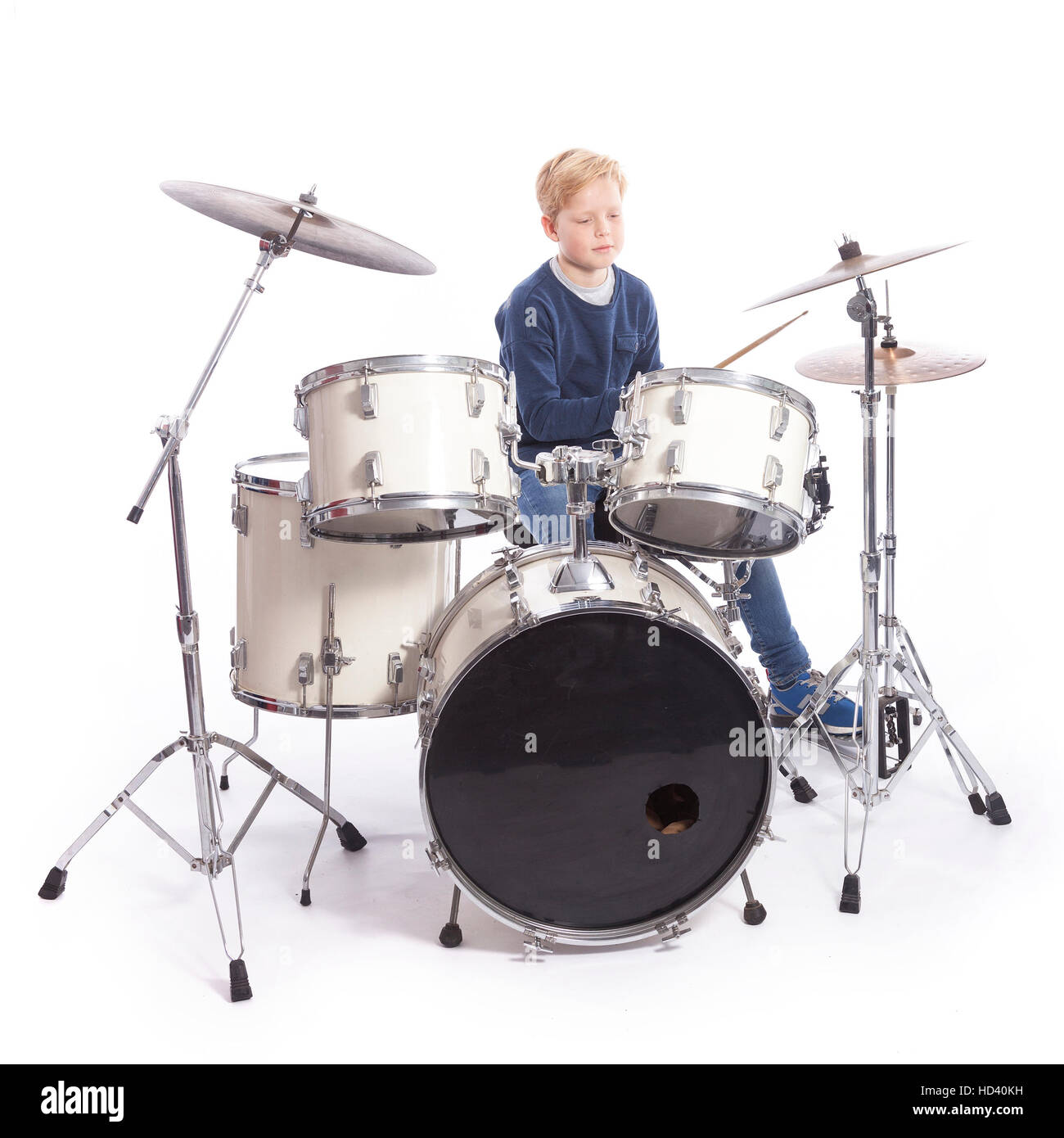 young blond boy drums behind drum kit against white background in ...
