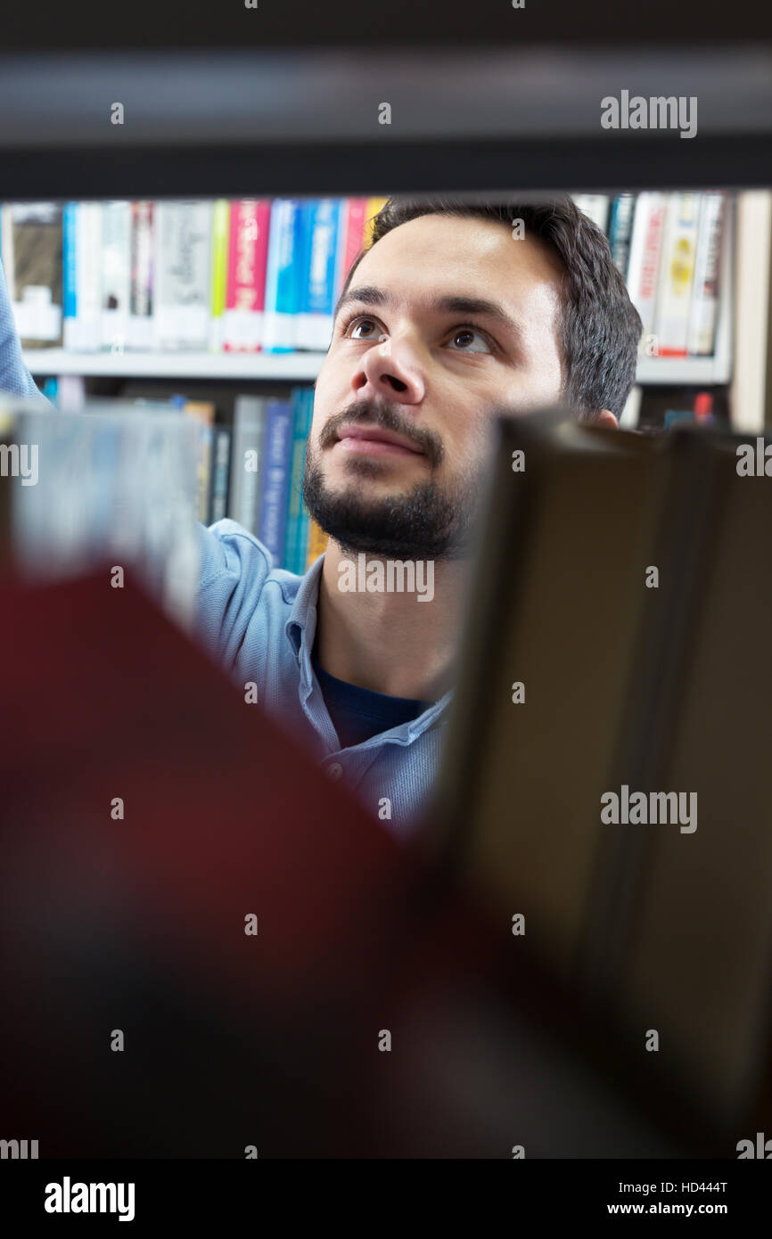 male college student taking book from shelf in library Stock Photo - Alamy