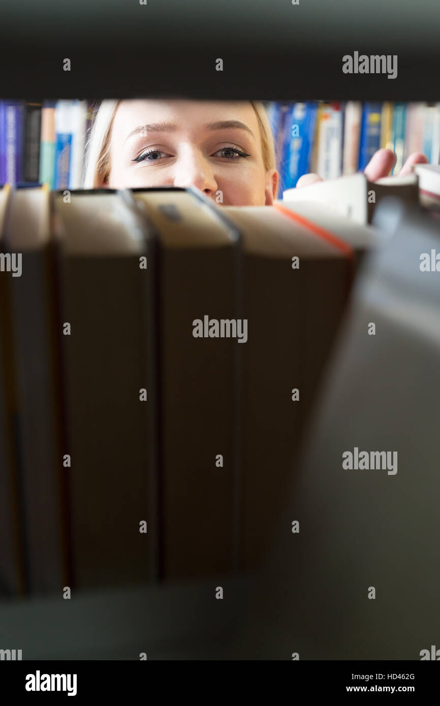 Student in library - cheerful woman look through bookshelf, hold book ...