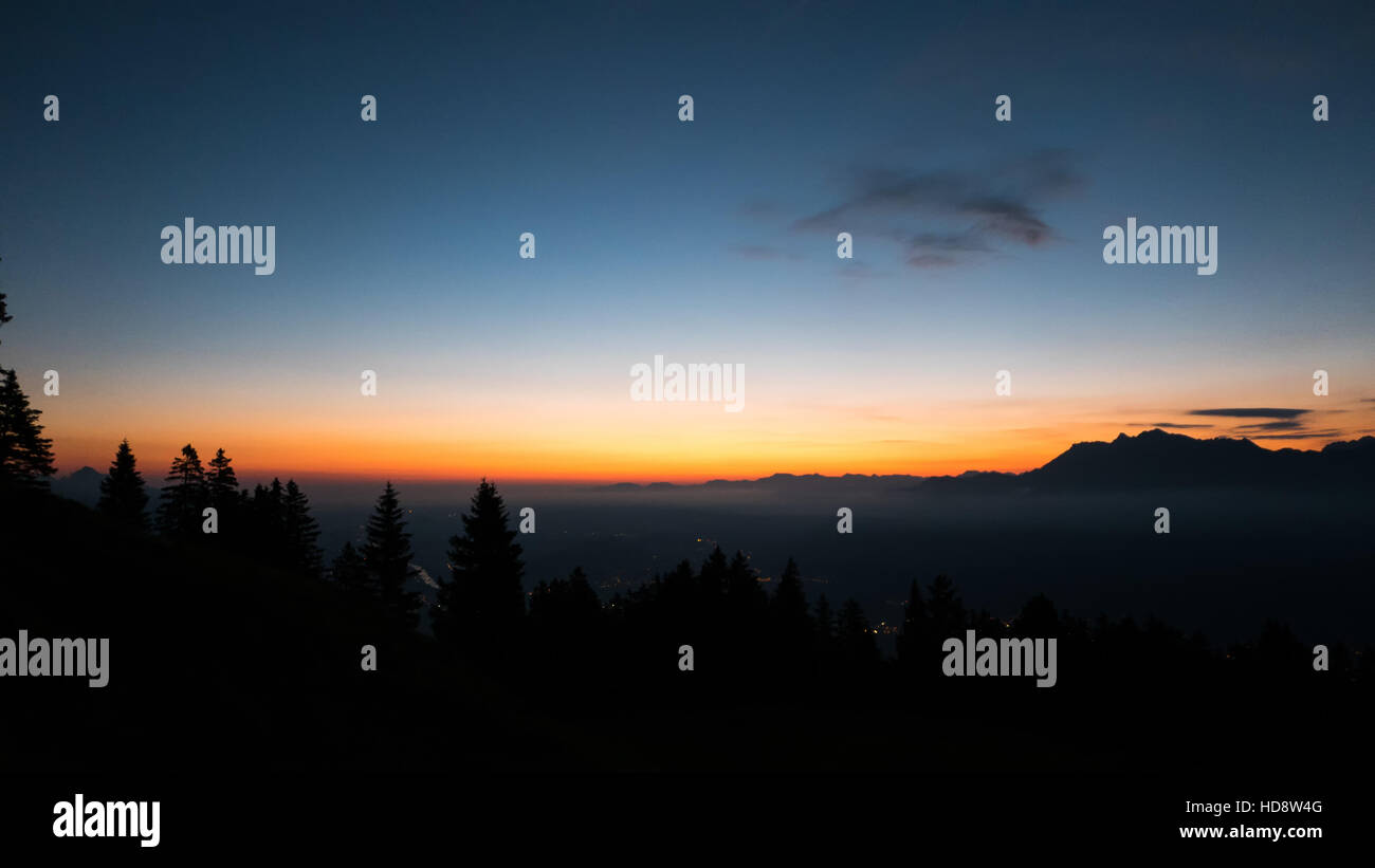A golden sunset rising through the trees in a forest over the valley in ...