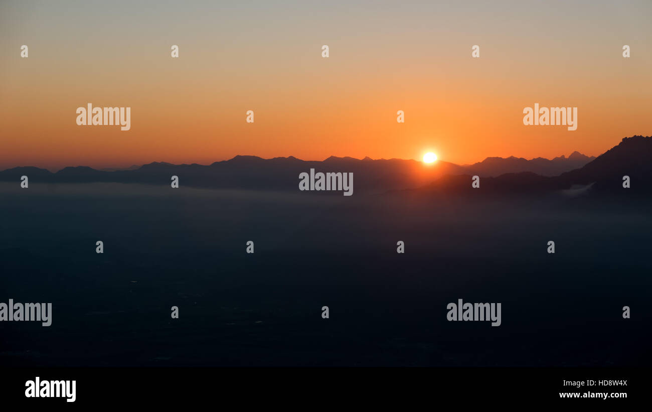 A golden sunset rising through the trees in a forest over the valley in ...