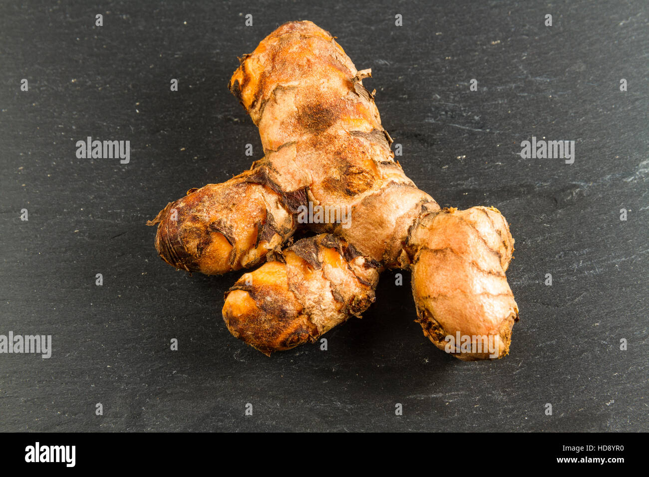 Piece of turmeric or Curcuma longa root on slate background, macro ...