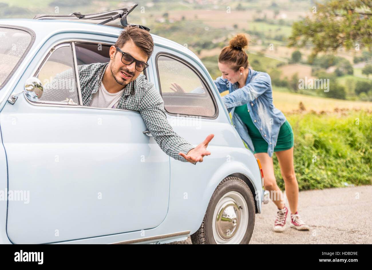 Engine break down.Strong young woman pushing a vintage car while man is ...