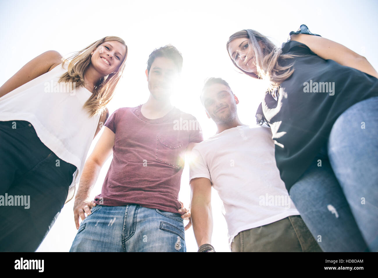 Four young people looking down at camera with backlight and sunflare ...