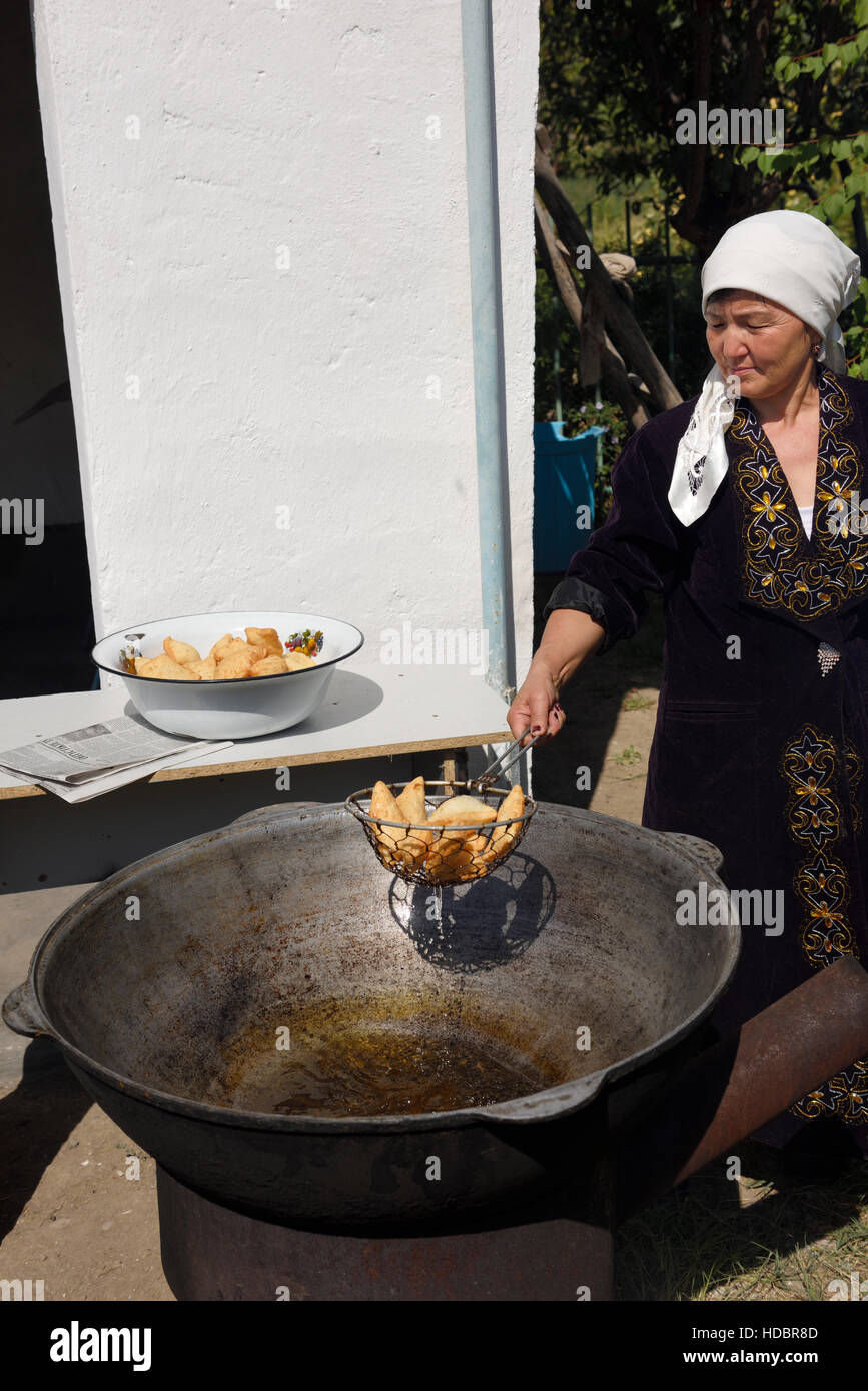 Kazakh woman in hajib draining Baursaki fried dough outdoors in ...