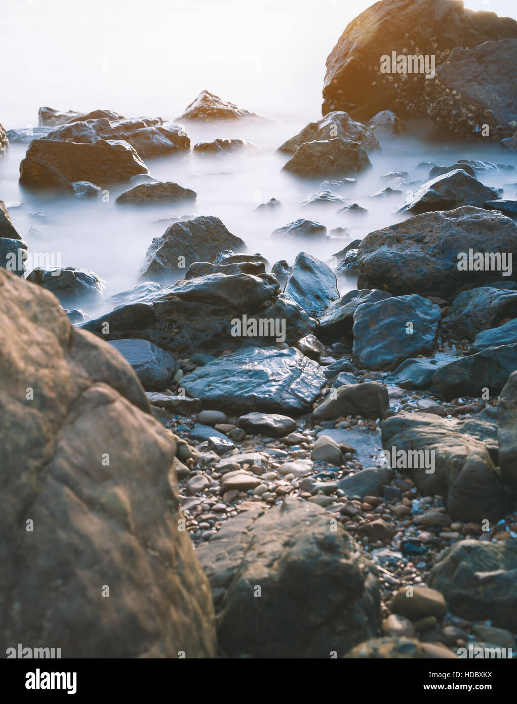 Vertical scene of black beach rock with milky wave and soft sunlight ...