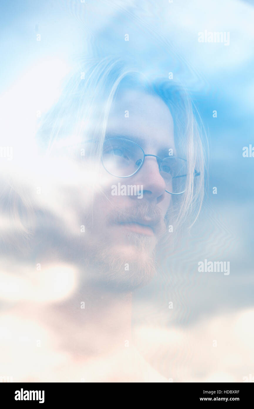 handsome young man looking out of window with reflection of cloudy sky ...