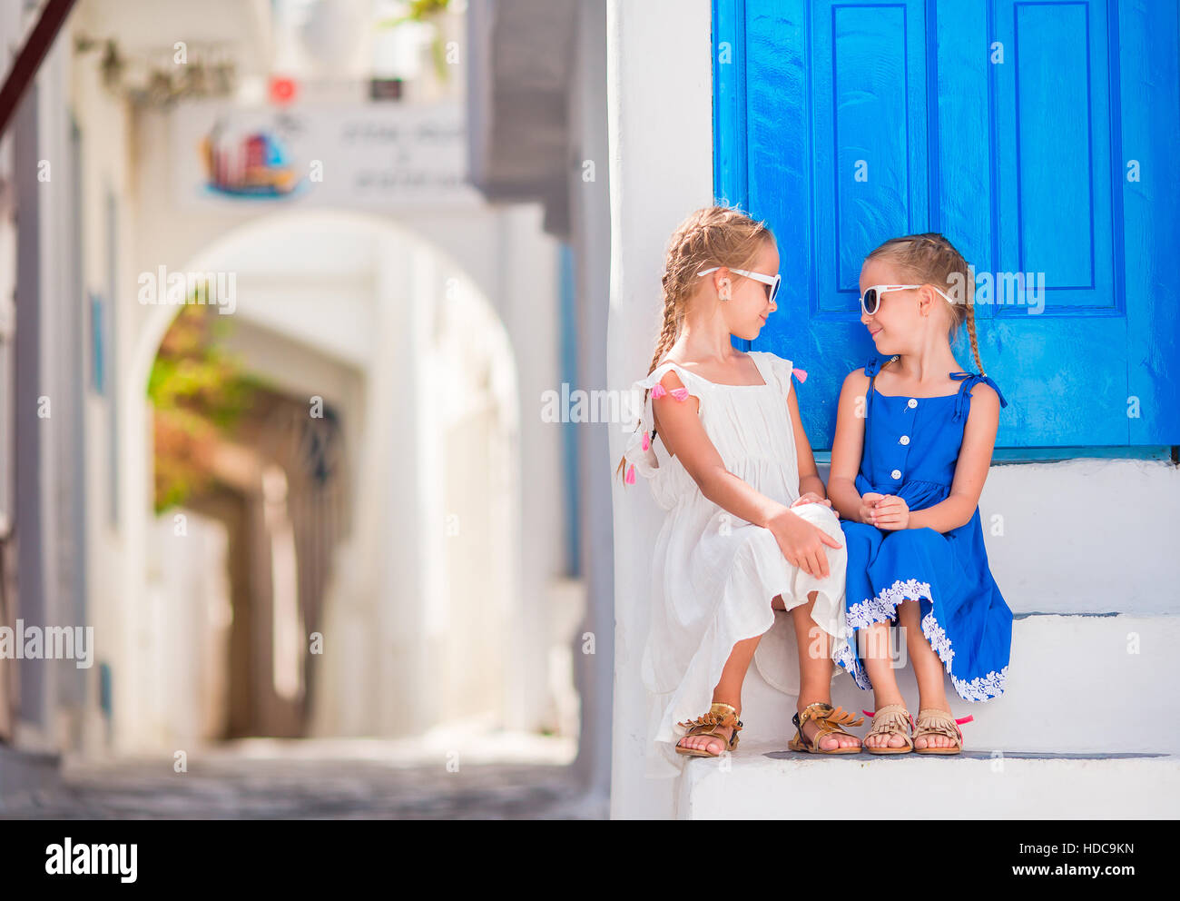 Little happy girls in dresses at street of typical greek traditional ...