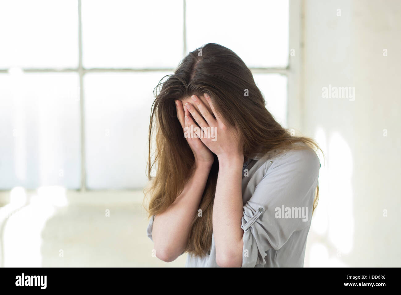 Young woman hiding face with hands indoors Stock Photo - Alamy