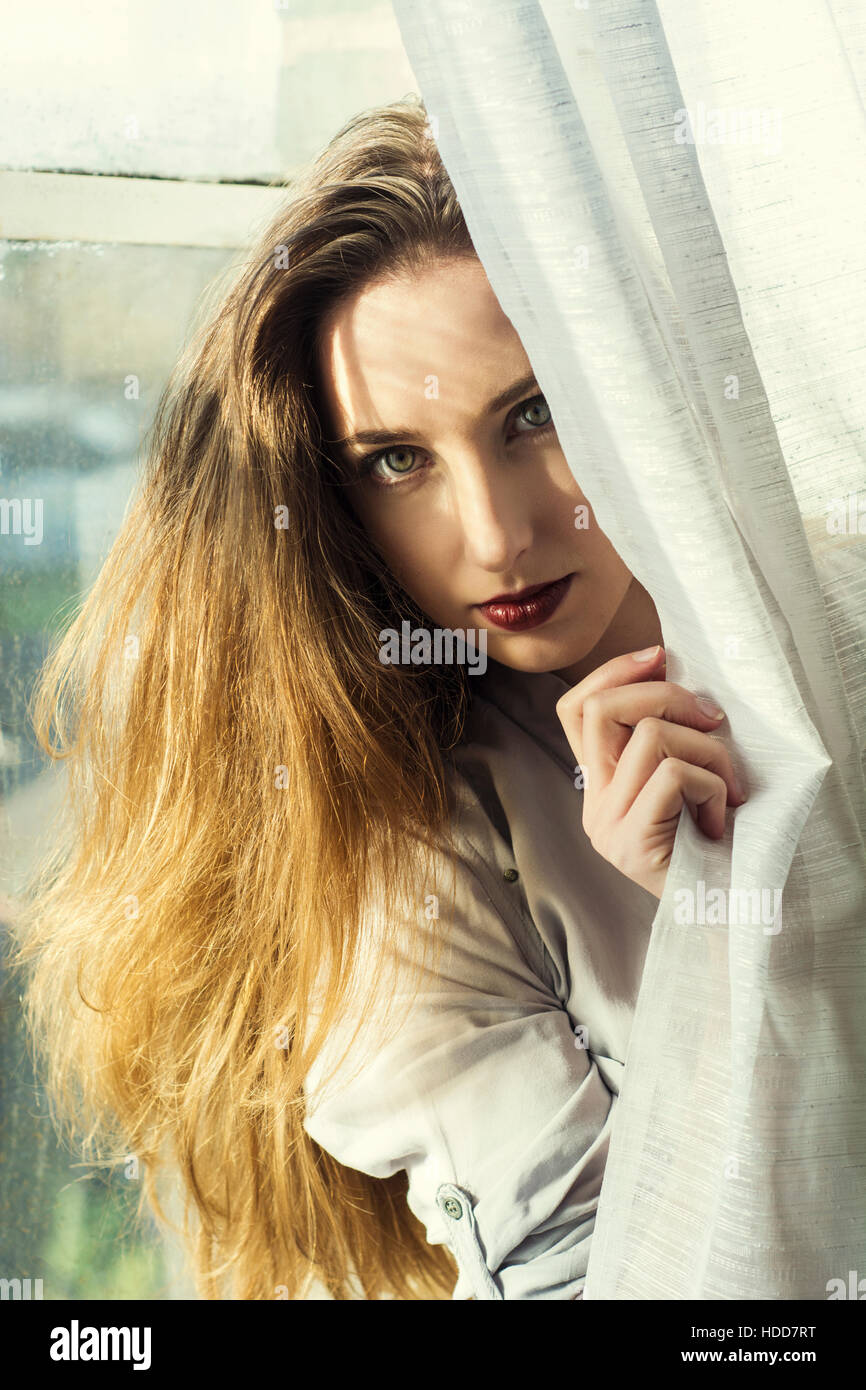 Beautiful young woman hiding behind the blinds Stock Photo - Alamy