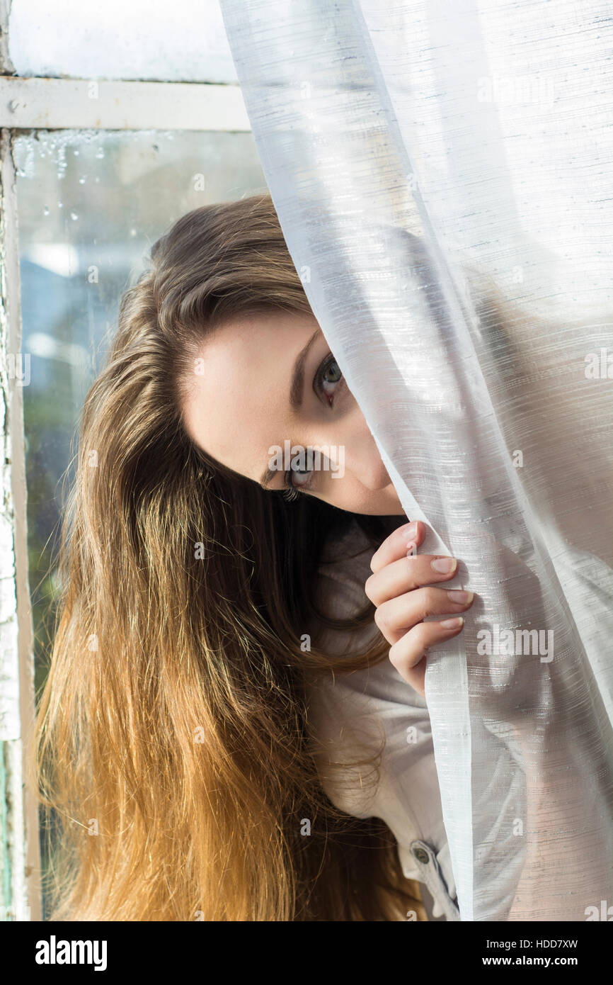 Beautiful young woman hiding behind the blinds Stock Photo - Alamy