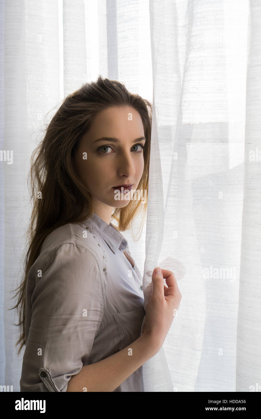 Beautiful young woman standing by the window Stock Photo - Alamy