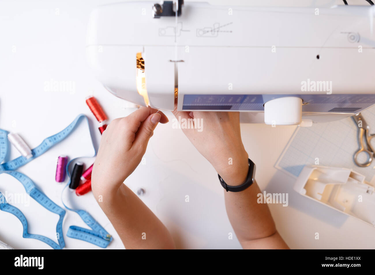 Woman sets up sewing machine on table with thread, scissors, measuring ...