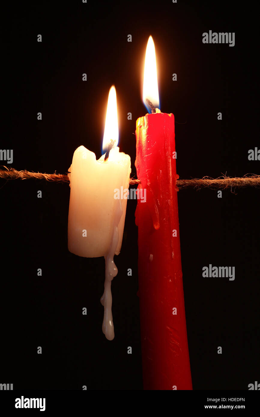Pair of lighting candles hanging with rope against dark background ...