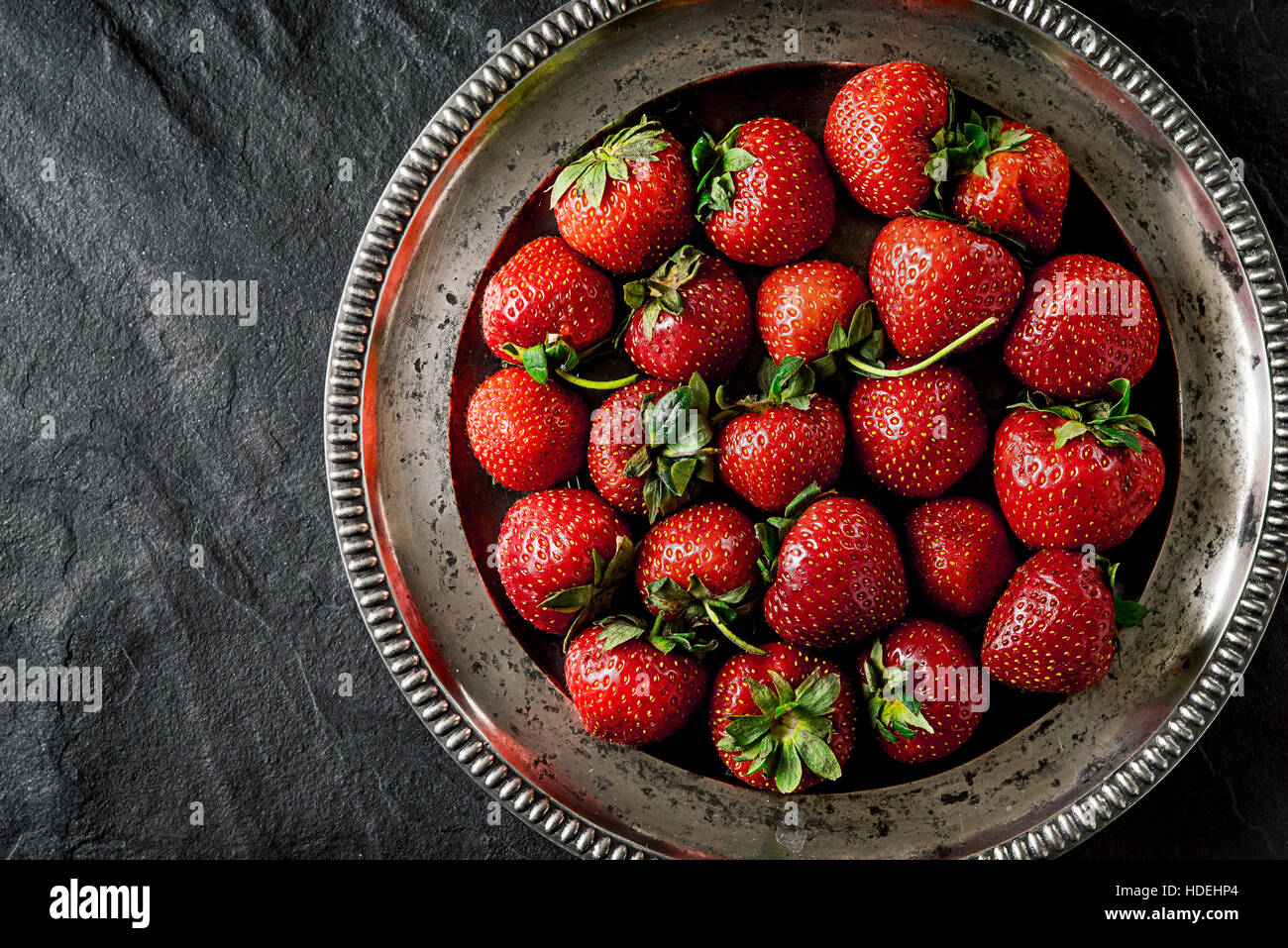 Strawberry in the old metal plate on the black stone table top view ...