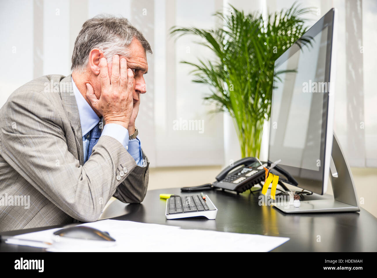 Pensive senior man looking at computer with concentration in his office ...