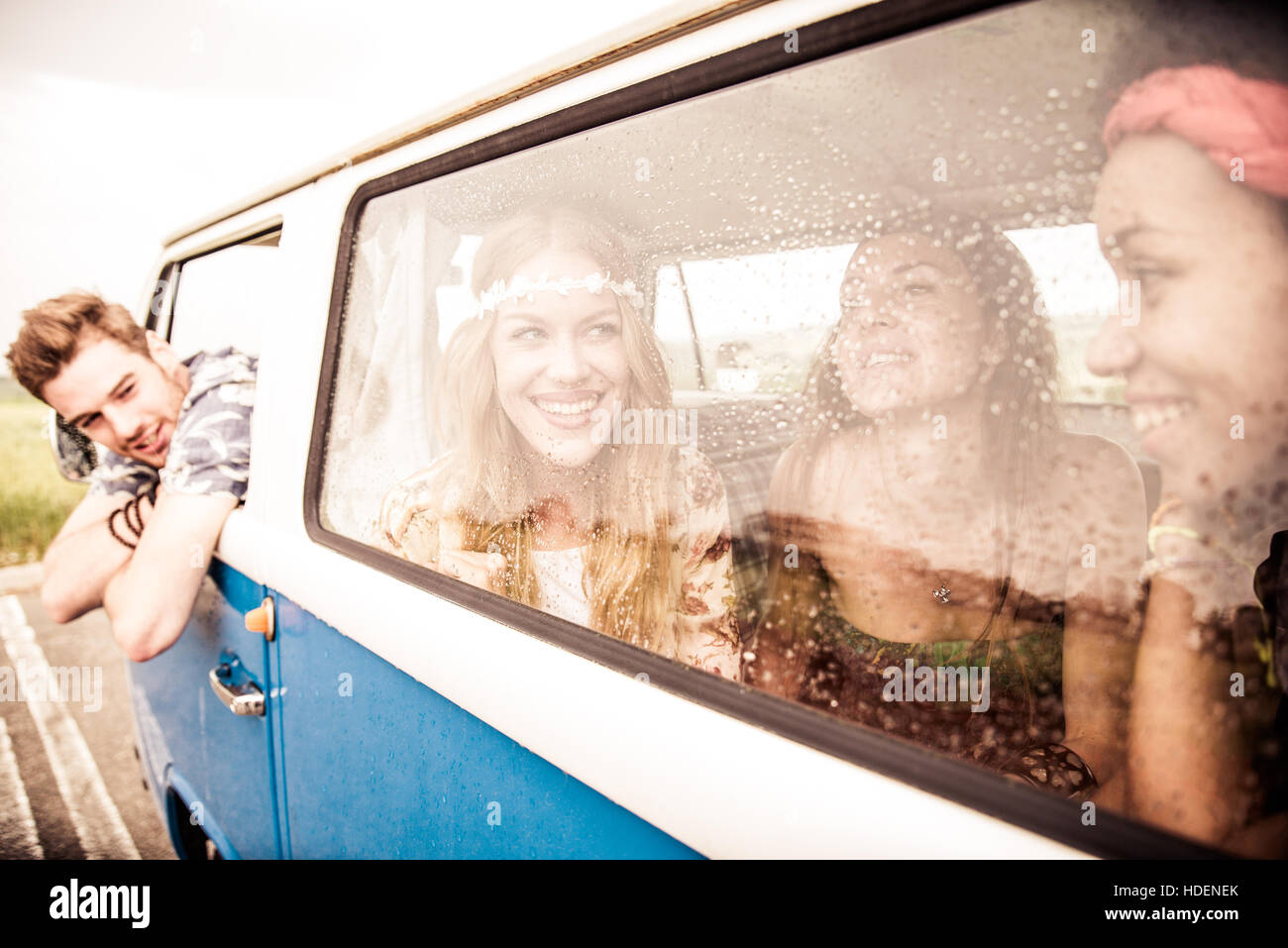 Friends in a 70's styled minivan repairing from summer rain, girls are ...