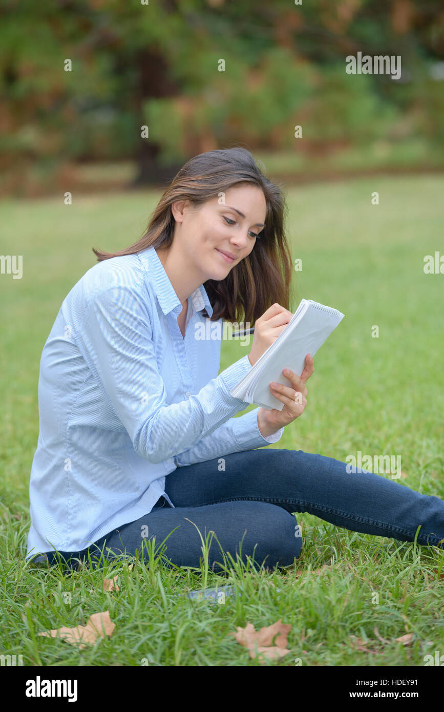 Woman sat in park writing in notepad Stock Photo - Alamy