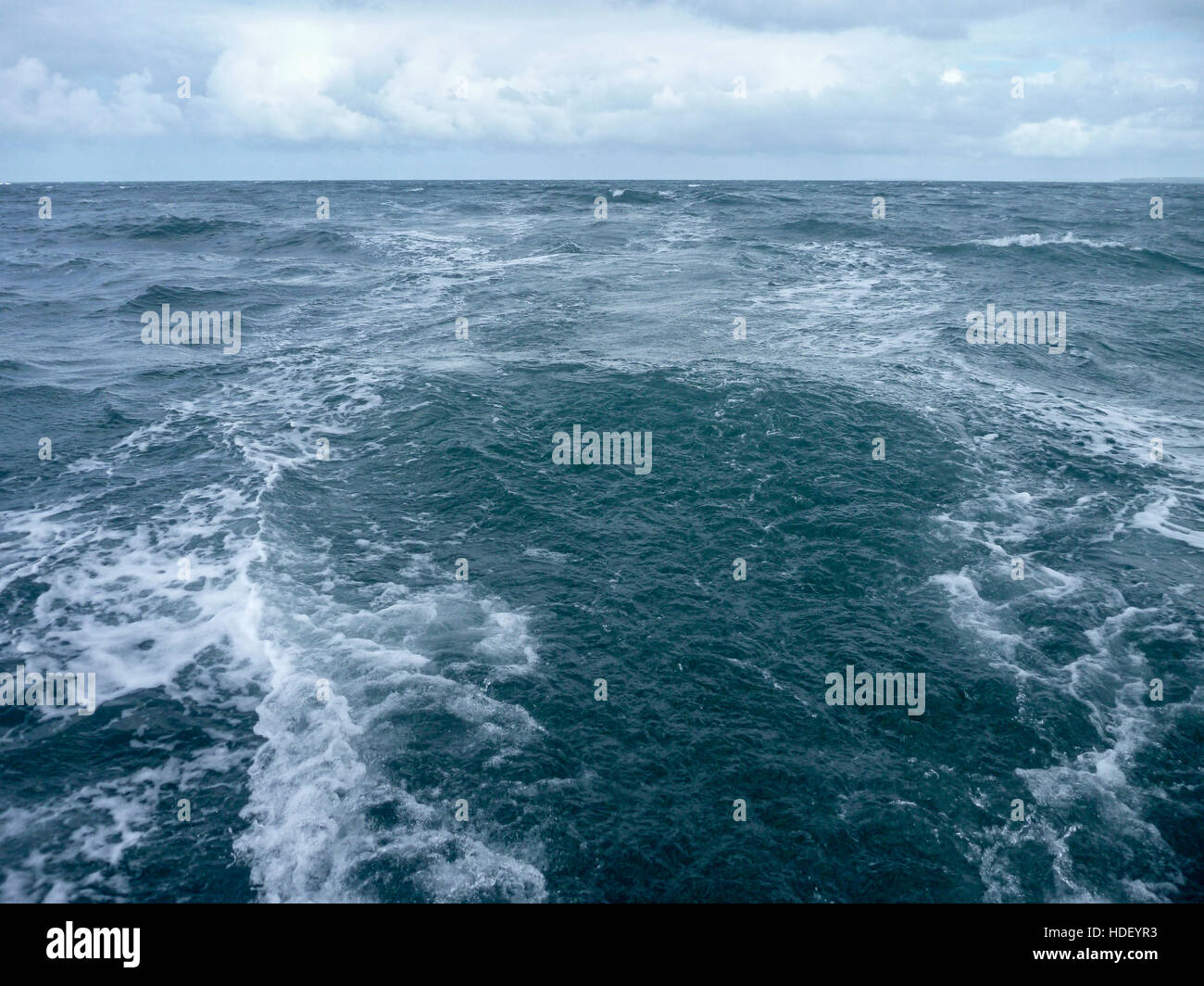 Wake of a yacht in a following green sea, weak blue sky with white ...