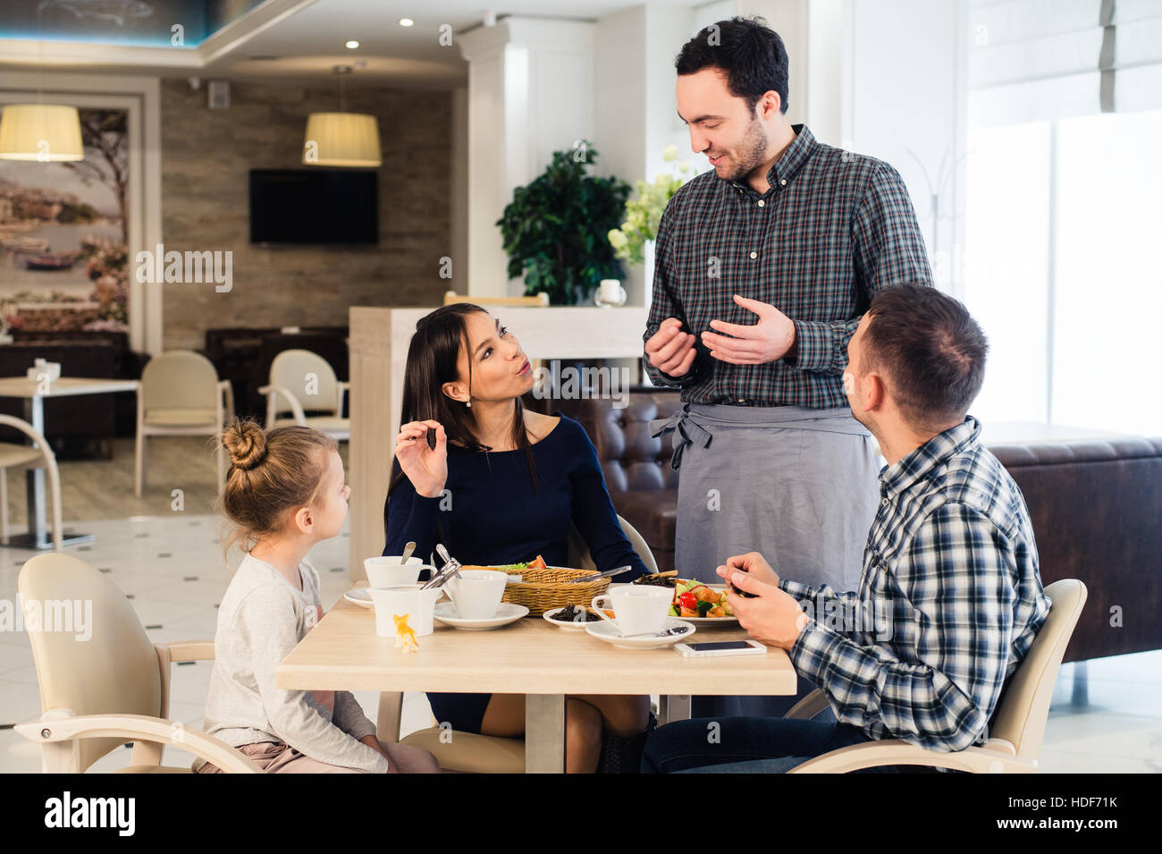 Friendly smiling waiter taking order at table of family having dinner ...