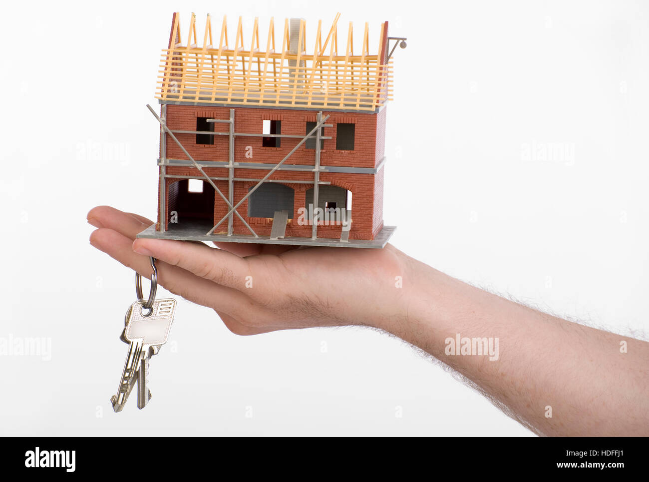Model of a house under construction and keys held in a hand, symbolic image for building a house ...