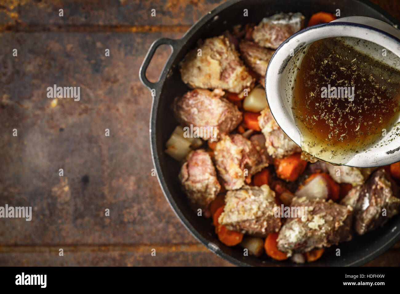 Adding broth in the pan with meat and vegetable top view Stock Photo ...