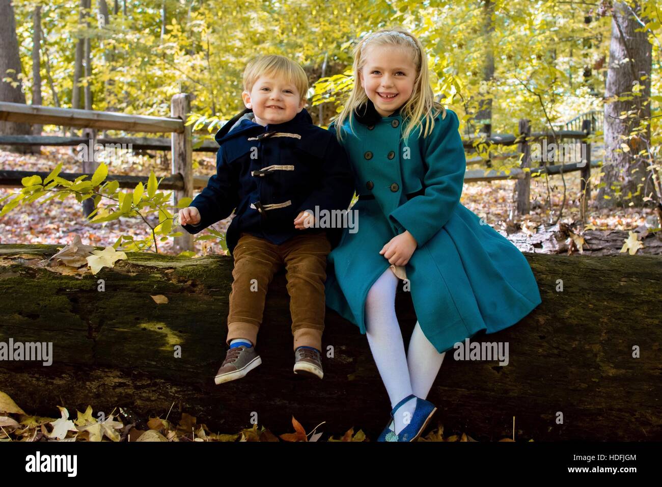 adorable brother and sister siblings sitting in winter coats in woods ...