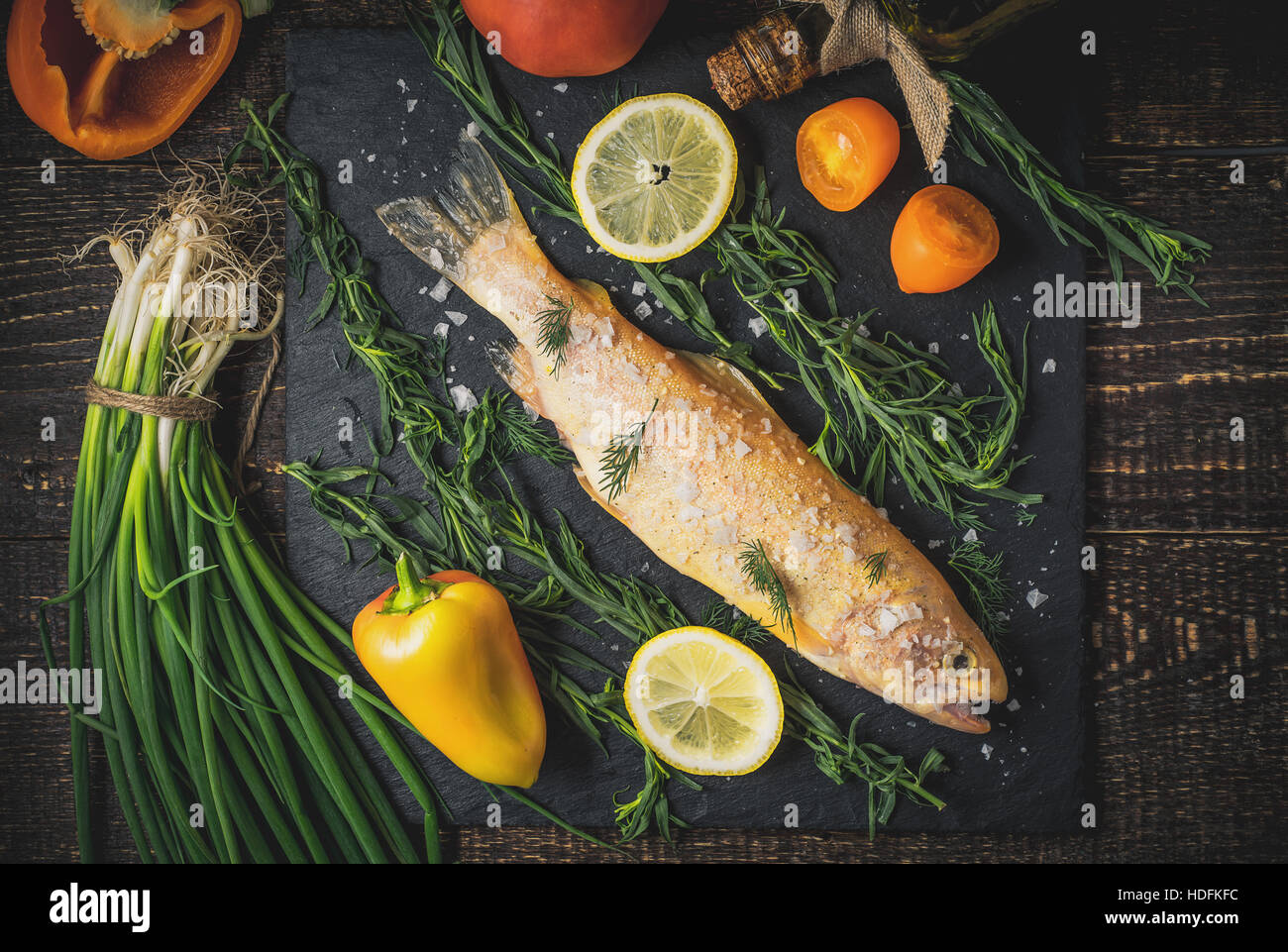 Raw golden trout with salt and vegetables on the wooden table top view ...