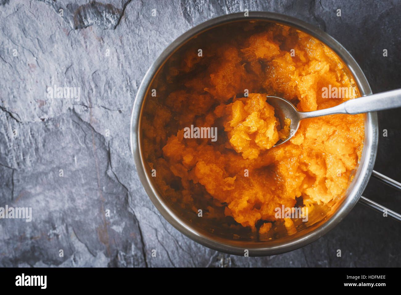 Pumpkin puree in the pot with spoon in the stone background top view ...